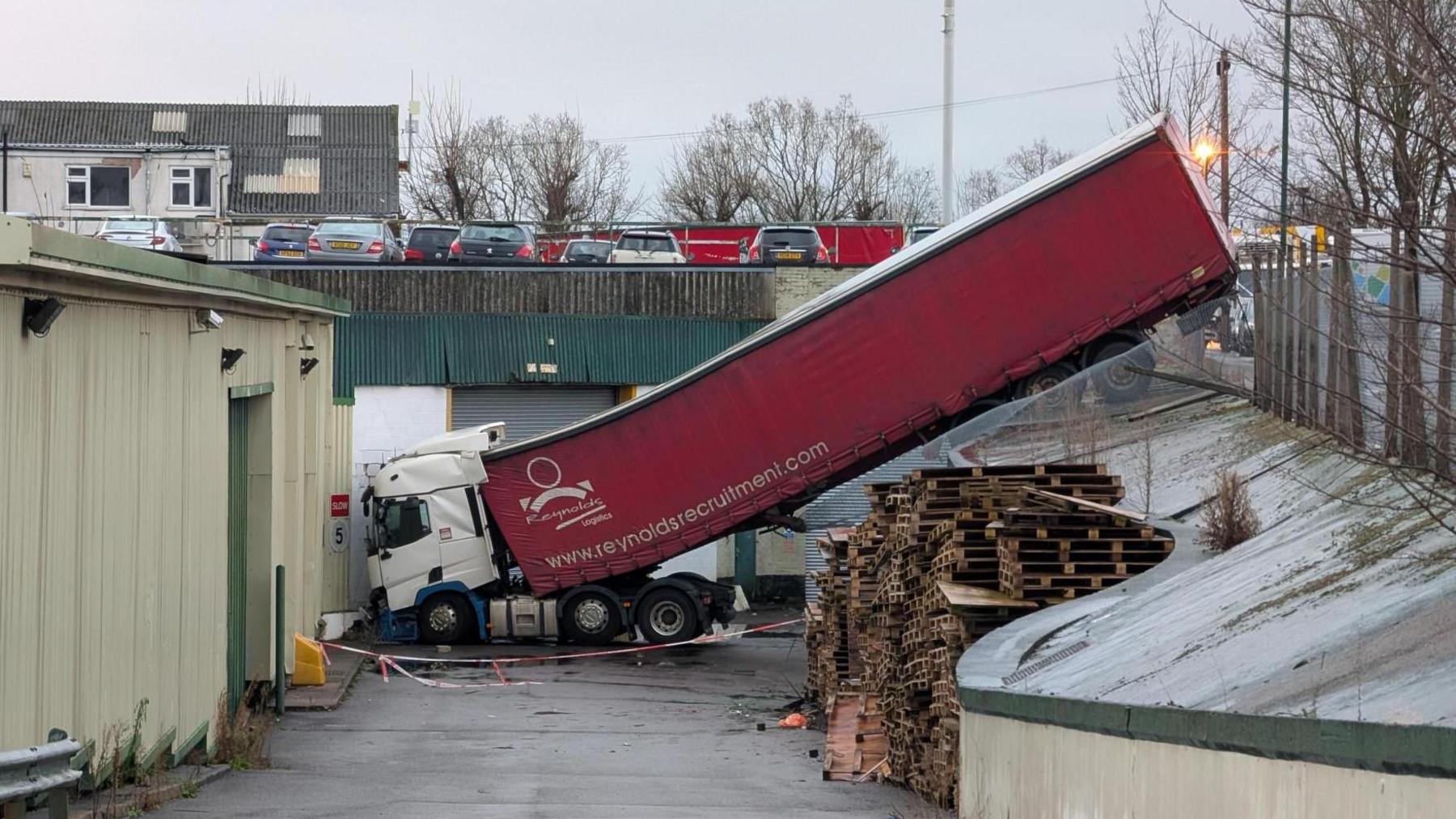 Lorry becomes stuck after smashing through fence - BBC News