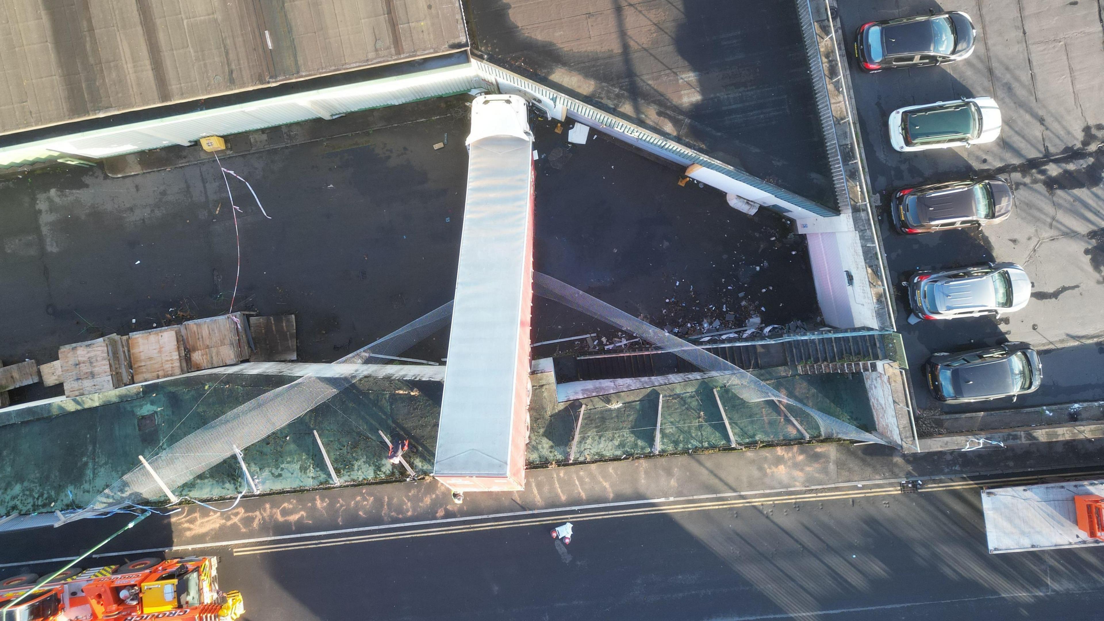 Lorry stuck on steep slope after smashing through fence - BBC News