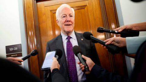 Man in suit stands before microphones
