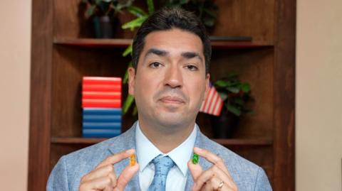 Bernd Debusmann holding up two gummy sweets. One is green and the other is orange.