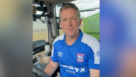 A man wearing an Ipswich Town shirt while sitting in a tractor. 