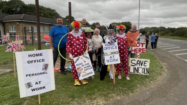 RAF Scampton asylum plan opponents stage 'clown' rally at site - BBC News