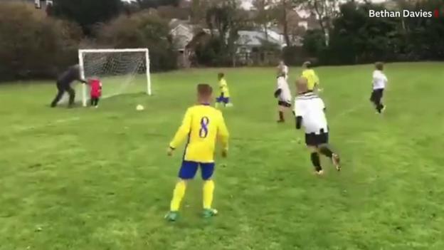 Video of 'pushy' dad helping son save goal goes viral - BBC News