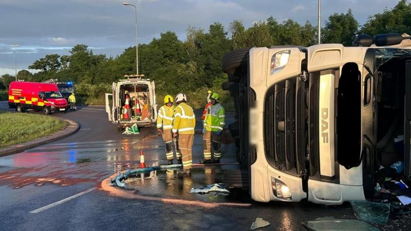 M40: Lorry carrying water tips over blocking slip road - BBC News