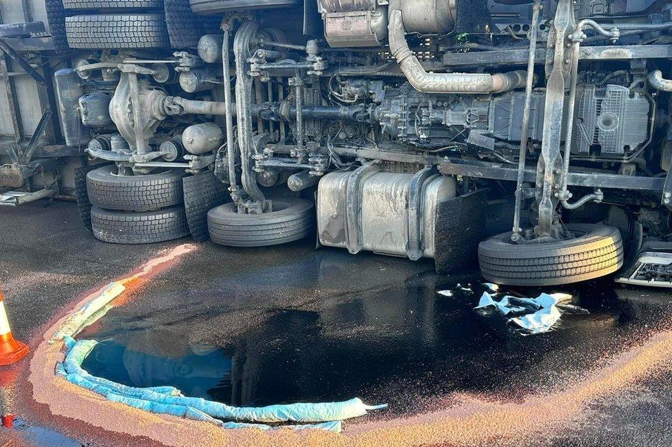 M40: Lorry carrying water tips over blocking slip road - BBC News