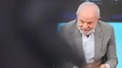 Lula, sentado, olha para o canto inferior esquerdo da imagem