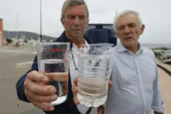 Rogliano's Mayor Patrice Quilici (L) and Tomino's Mayor Francois Orlandi (2L) hold a glass of brine and a glass of sea water respectively as they stand in front of a desalination plant at Macinaggio Port in Rogliano on the French island of Corsica, on October 12, 2022.