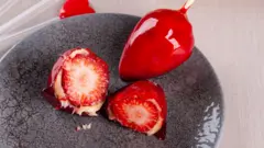 Morangos cobertos com brigadeiro branco e envoltos por uma camada espessa de caramelo vermelho brilhante