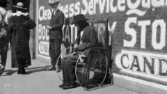 Un anciano en silla de ruedas pidiendo limosna en 1910