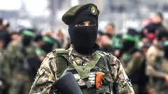 Armed fighters from Hamas' Izz ad-Din al-Qassam Brigades stand guard during the handover of three Israeli hostages to Red Cross representatives in Al Nuseirat refugee camp, central Gaza Strip, 22 February 2025