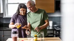 Una pareja en una cocina con varios frascos de pastillas deciden cuál tomar