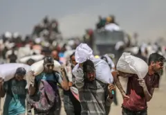 فلسطينيون يحملون أكياساً من الطحين بالقرب من نقطة توزيع المواد الغذائية، شمال قطاع غزة