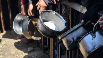 खाना पकाउने भाडाँ बोकेर बारमा उभिइरहेकाहरू