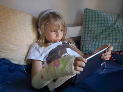 Uma criança sentada na cama com fones de ouvido e um iPad na mão