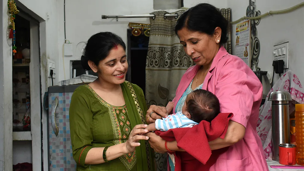 Two women holding hand fans, and a baby, sit on the street