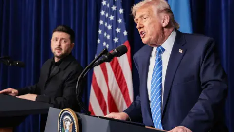 Ukrainian President Volodymyr Zelensky looks at US President Donald Trump as the pair stand behind separate podiums in front of US and Ukrainian flags