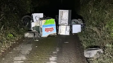 Fly-tipped waste blocks rural unlit road near Tregiskey