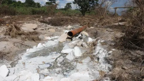 A picture of a pipe leading to a dry river. The rocks are covered in a white sediment