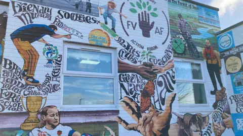A picture of a section of the mural that has a female rugby player, a butterfly near a hand, the FVAF logo, a biker, a man wearing a life jacket, a skate boarder and a ram.