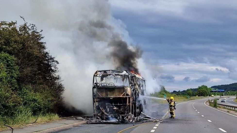Driver's lucky escape as coach engulfed in flames on major road - BBC News